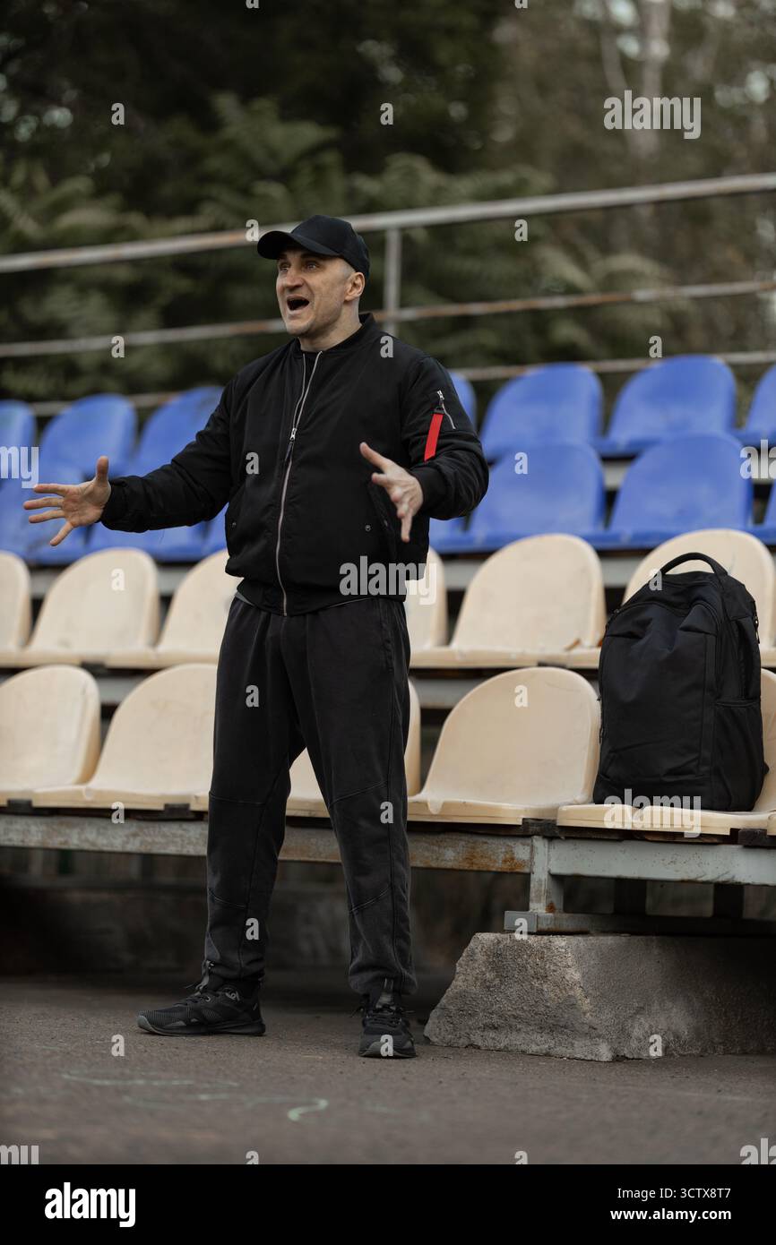 In a quiet stadium a man in a black bomber jacket and cap stands in the ...