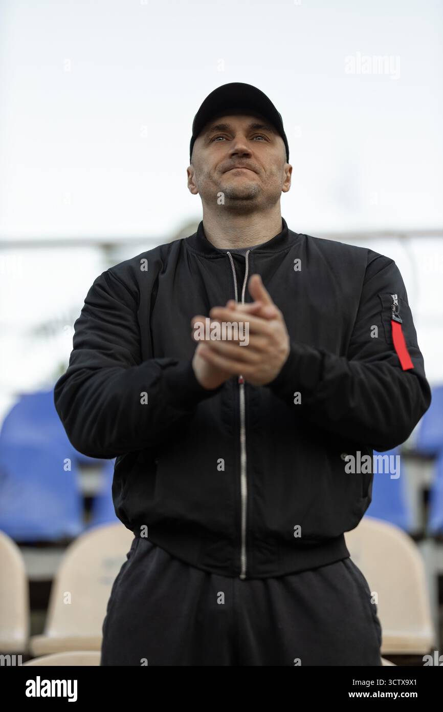 man wearing a black bomber jacket and cap stands in the empty stadium ...