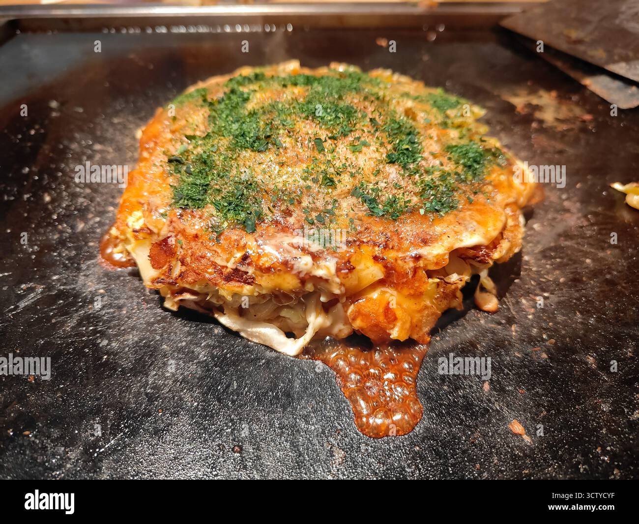 Traditional Japanese okonomiyaki being cooked on a teppan grill ...