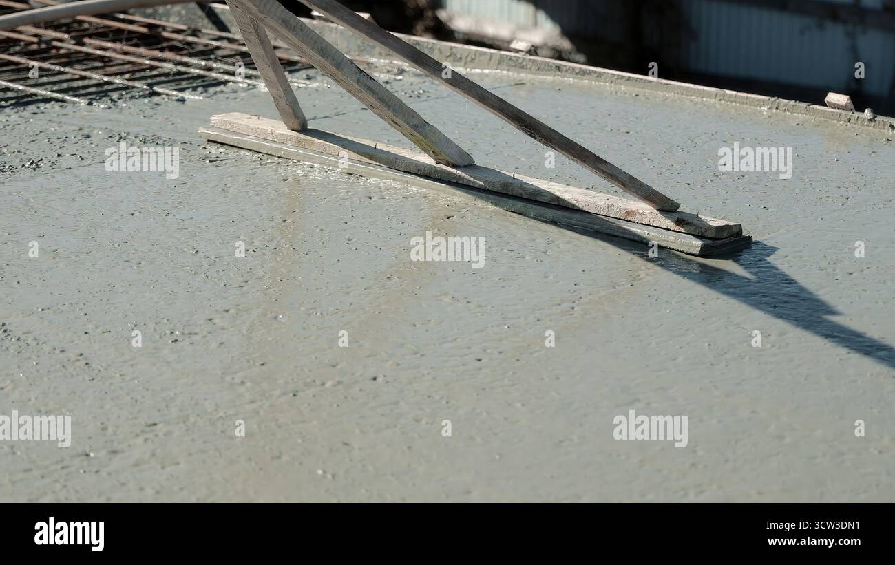 Leveling freshly poured concrete with screed tool. Close-up of a wooden ...