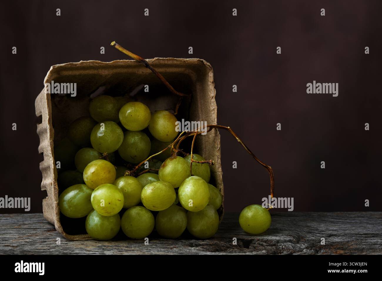 A bunch of green grapes in a cardboard produce box on a rustic wood ...