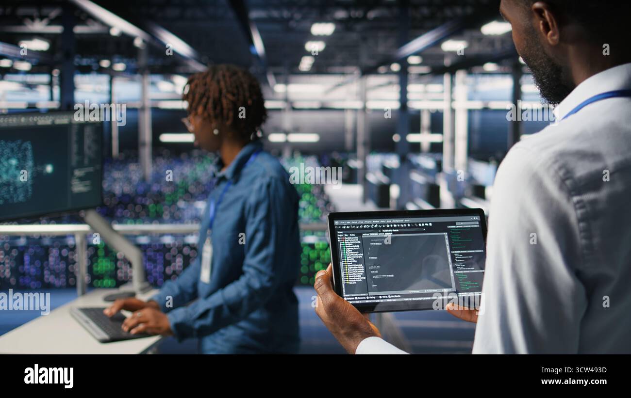 Data center admin checking code on tablet next to colleague reviewing ...