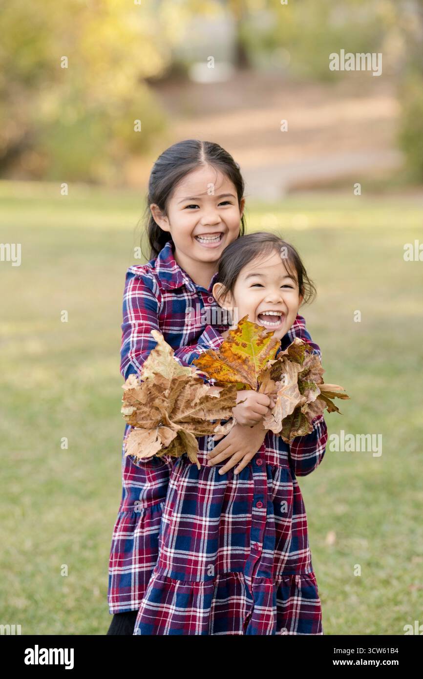 Sisters laugh and hug while holding autumn leaves Stock Photo - Alamy