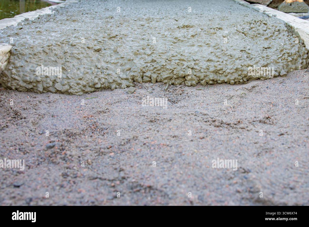 Fresh concrete being poured and leveled on a sandy surface near water ...