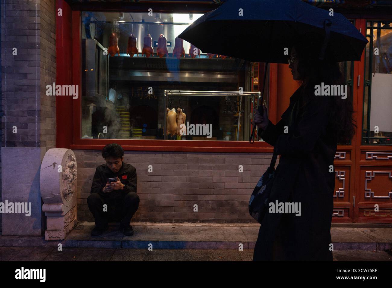 A restaurant worker takes a break to smoke near ducks hanging in a ...