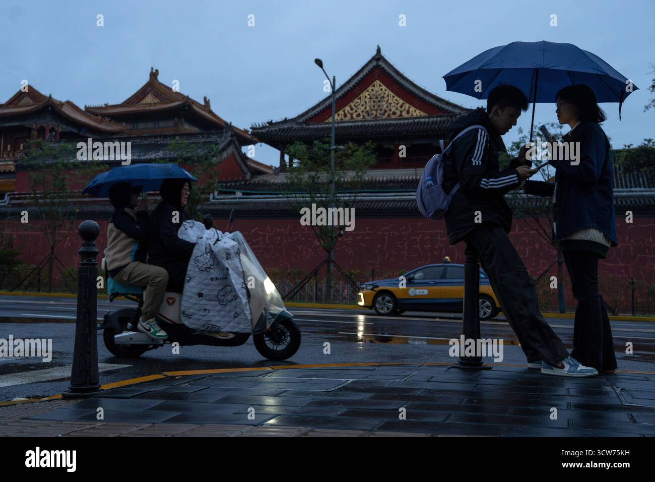 A couple chat as they share an umbrella during a rainy day in Beijing ...