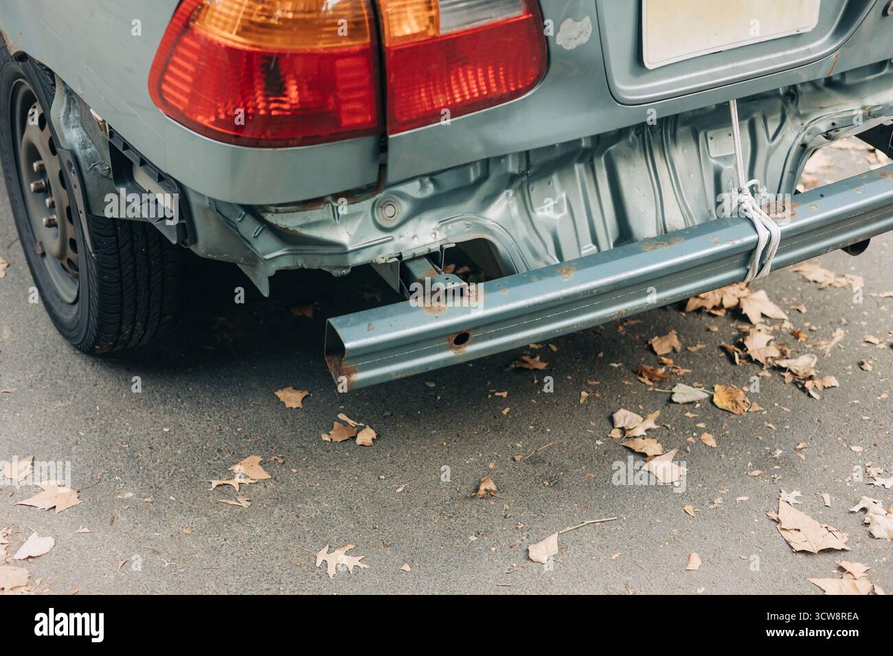A vehicle shows visible damage to the rear bumper with rust and leaves ...
