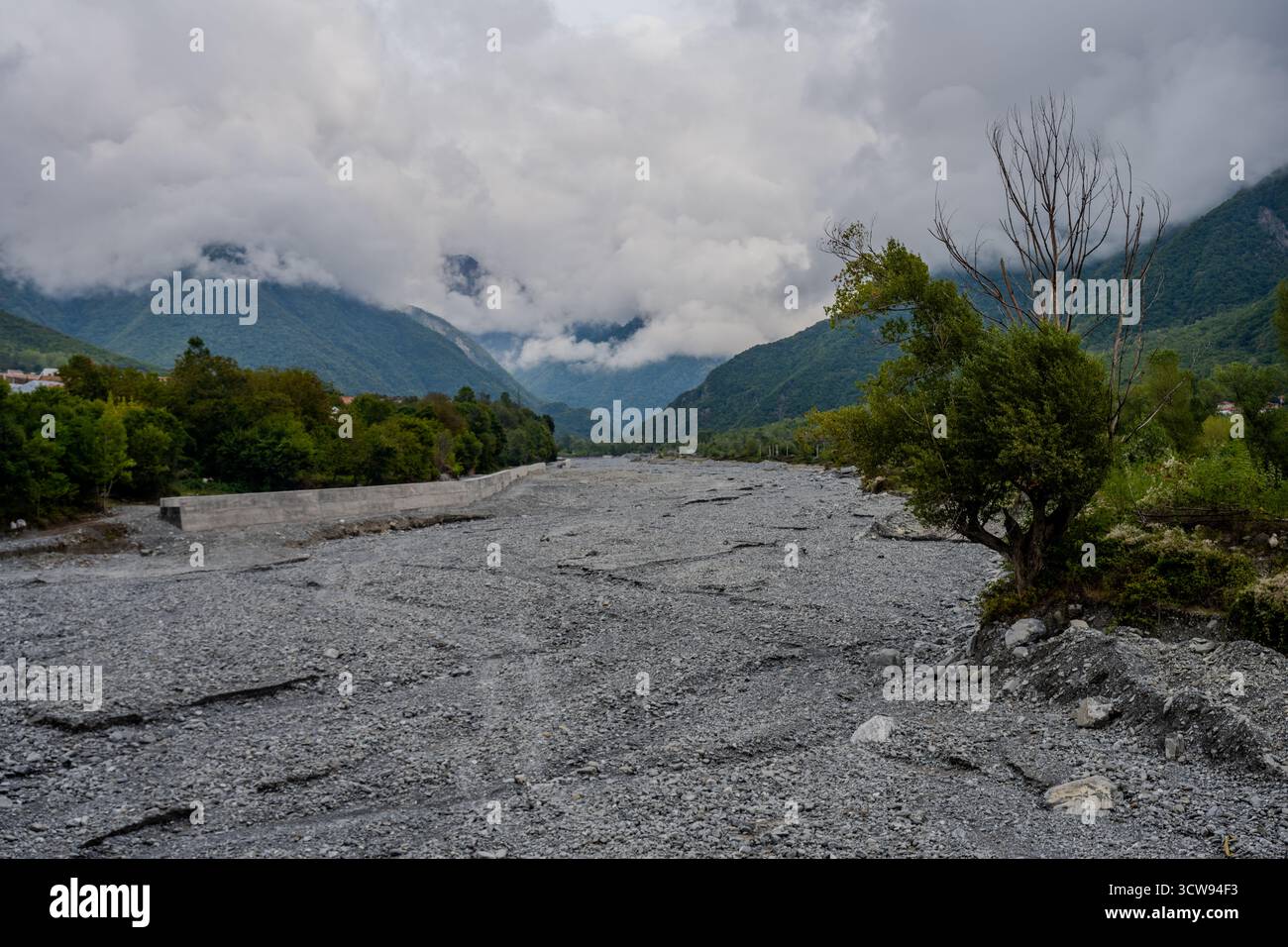 A wide dry riverbed stretches between forested mountain slopes near ...