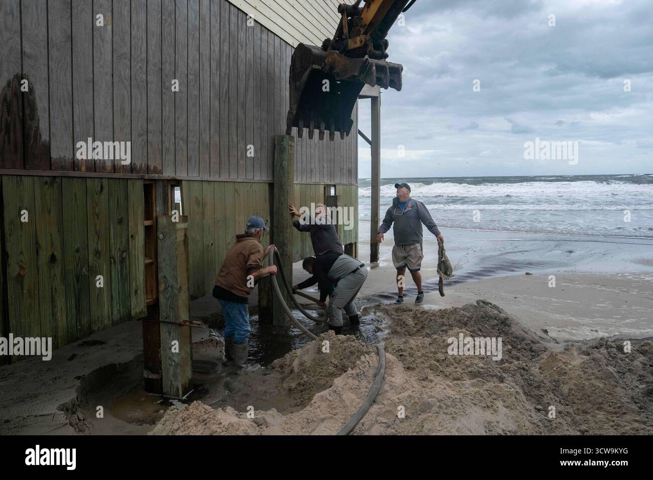 Workers put a piling into the ground to reinforce a home at risk of ...