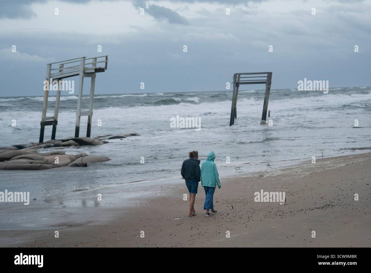At low tide people walk past the remains of homes, as a storm ...