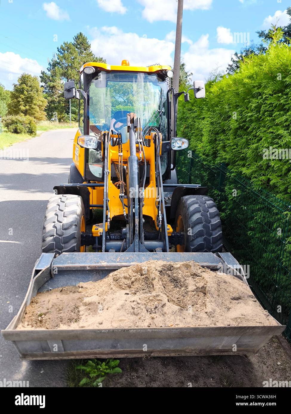 The construction loader is positioned on a paved road, its bucket ...