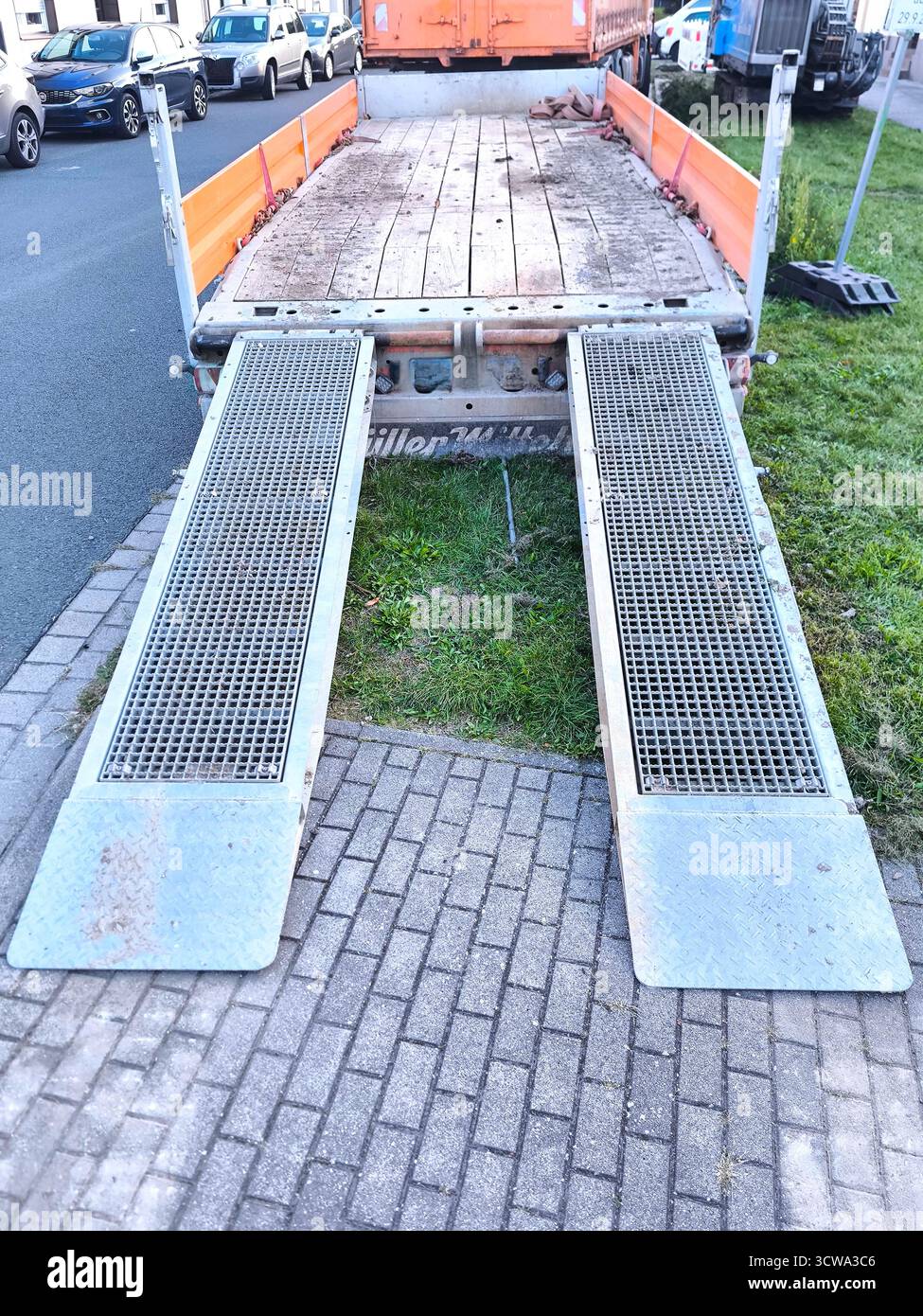 A low-sided cargo trailer equipped with two metal ramps with a mesh ...