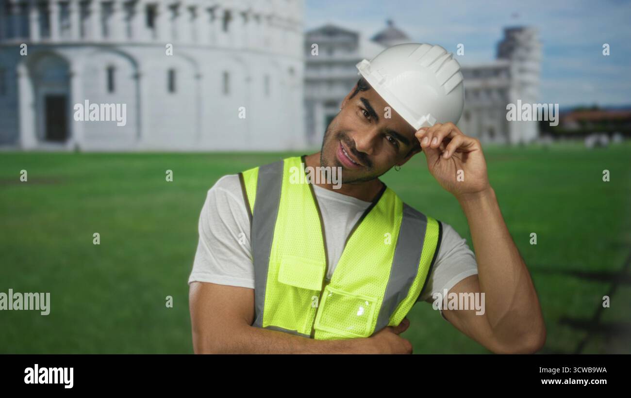 Man in yellow safety vest smiles and adjusts helmet with hand at leaning tower of pisa building ...