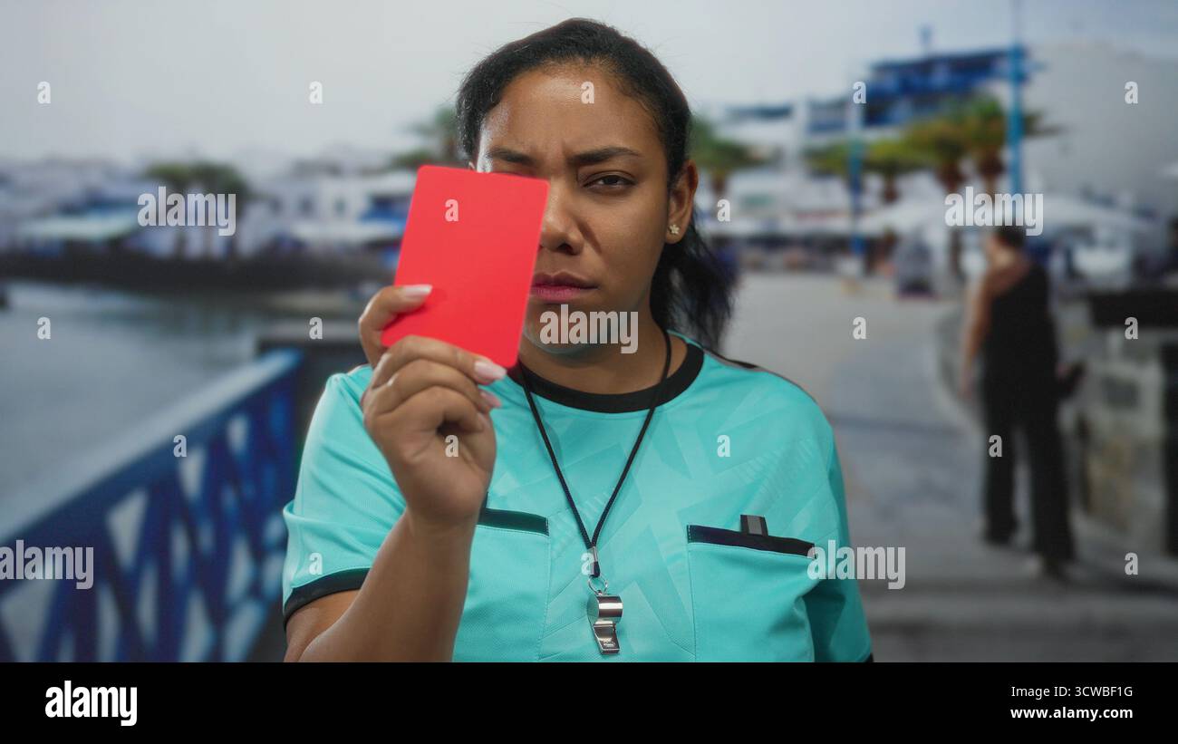 Woman referee on street by the sea holds red card at eye level with ...