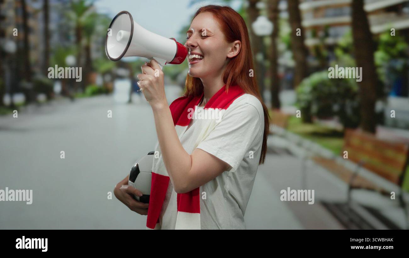 Woman cheering with megaphone and soccer ball on city street wearing ...