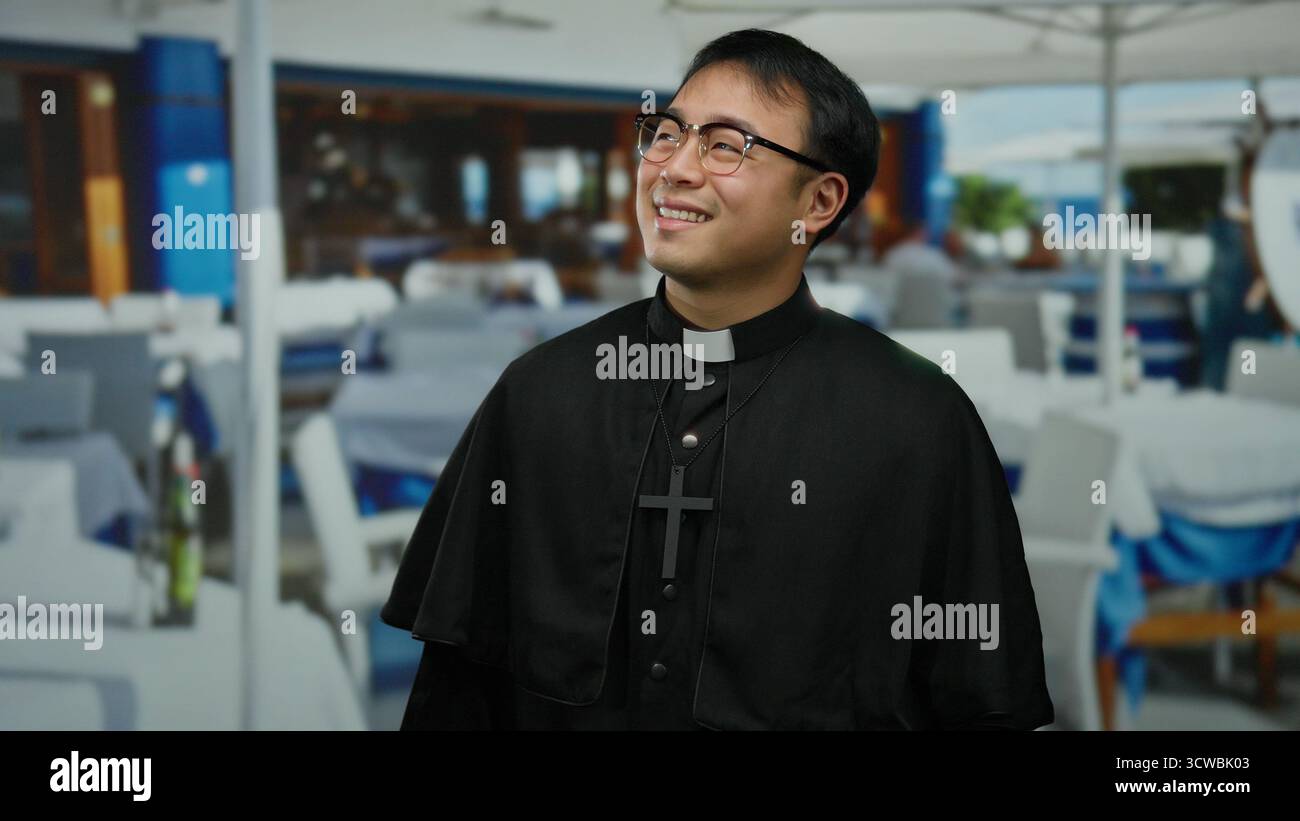 Smiling priest standing in an outdoor restaurant with blurred ...