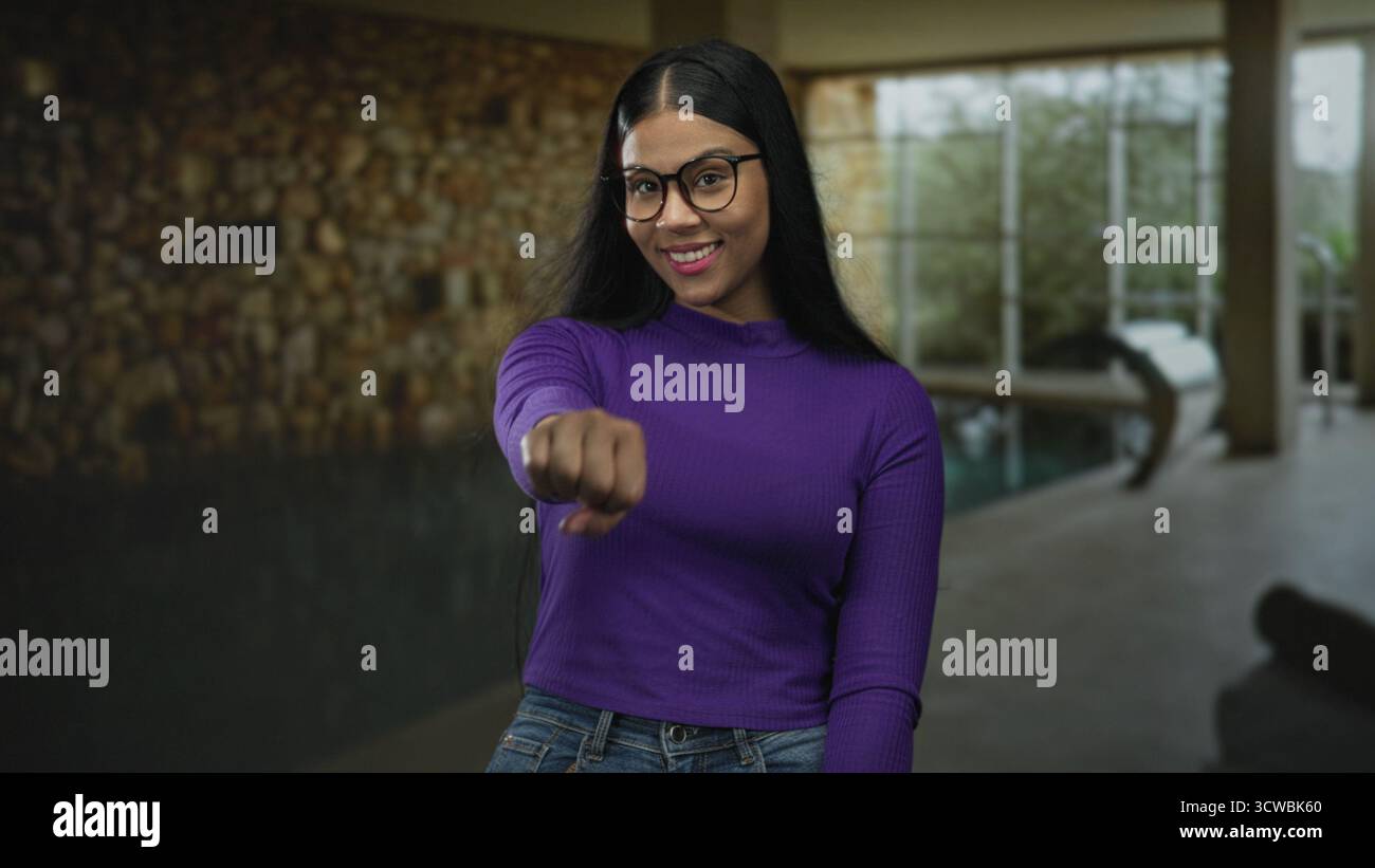 Latin woman wearing purple sweater raises fist over pool inside ...