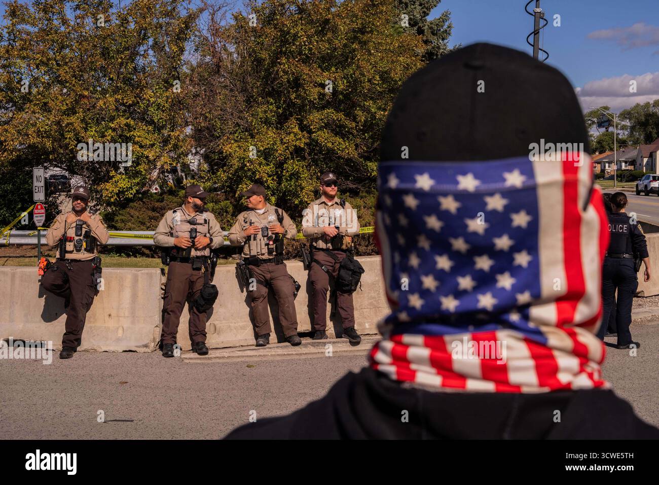 A protestor wearing an American flag face covering stands opposite Cook ...