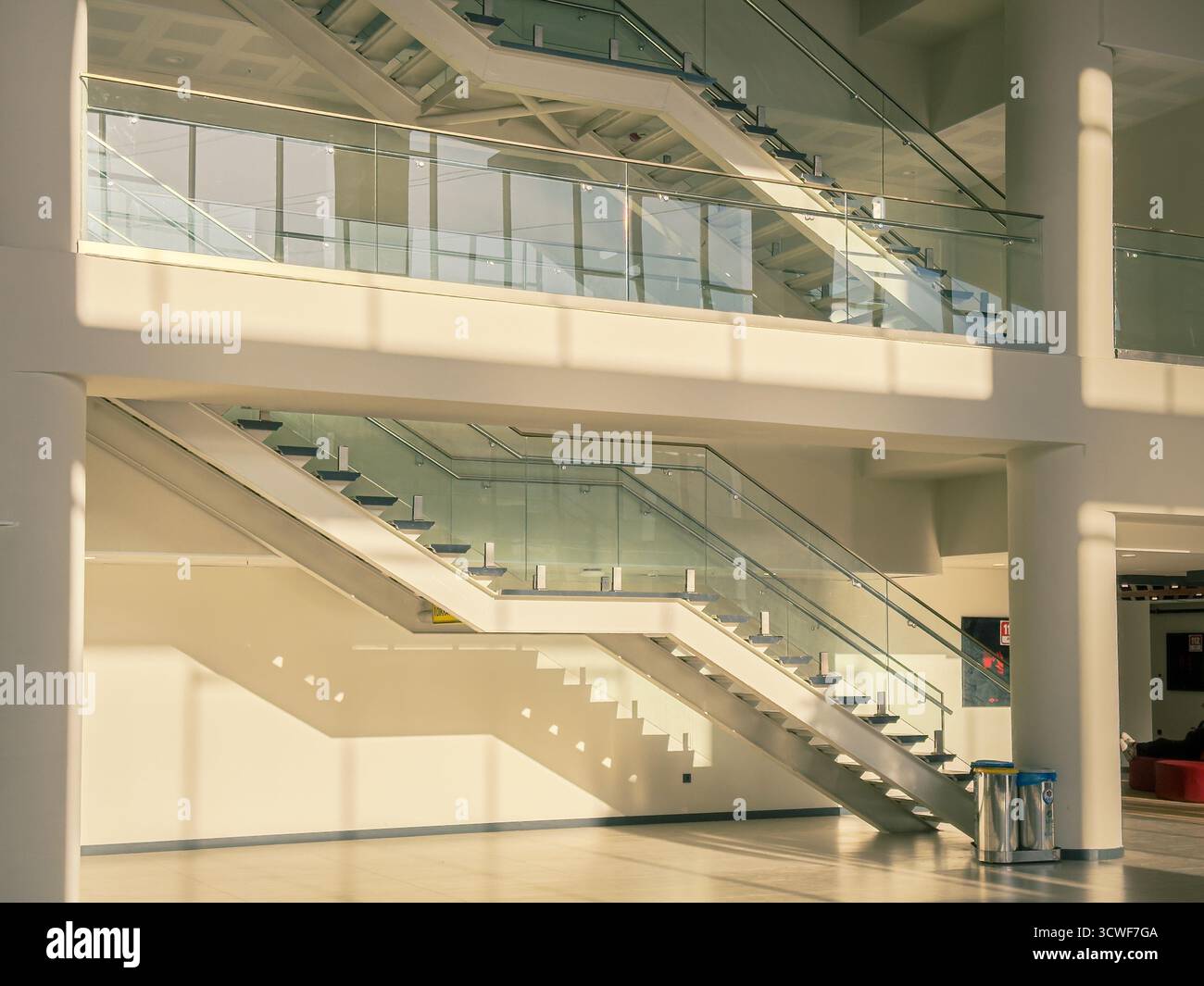 Modern glass staircases in bright indoor atrium with palm trees and sky ...