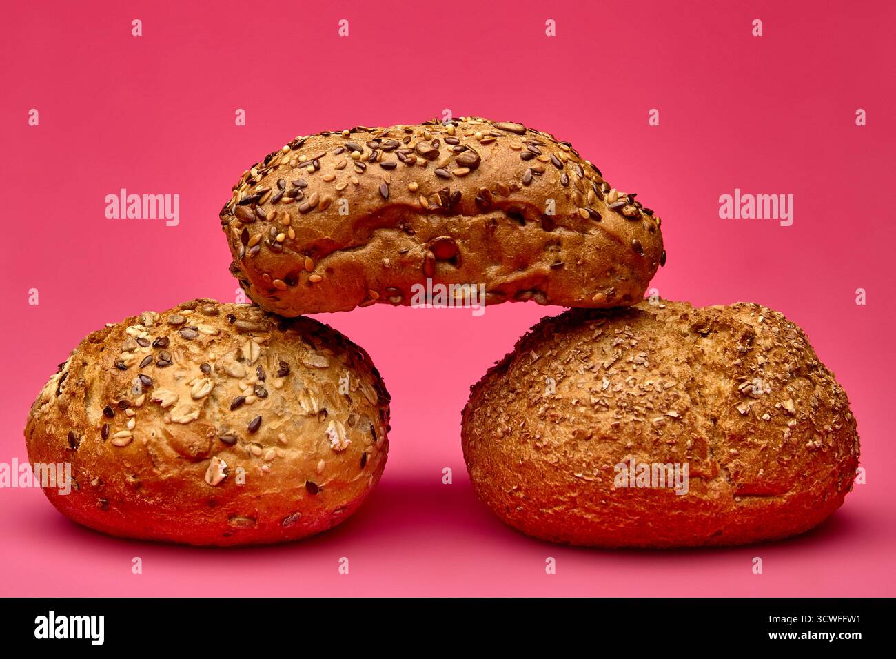 Two round buns supporting a seeded bread piece on a pink background ...