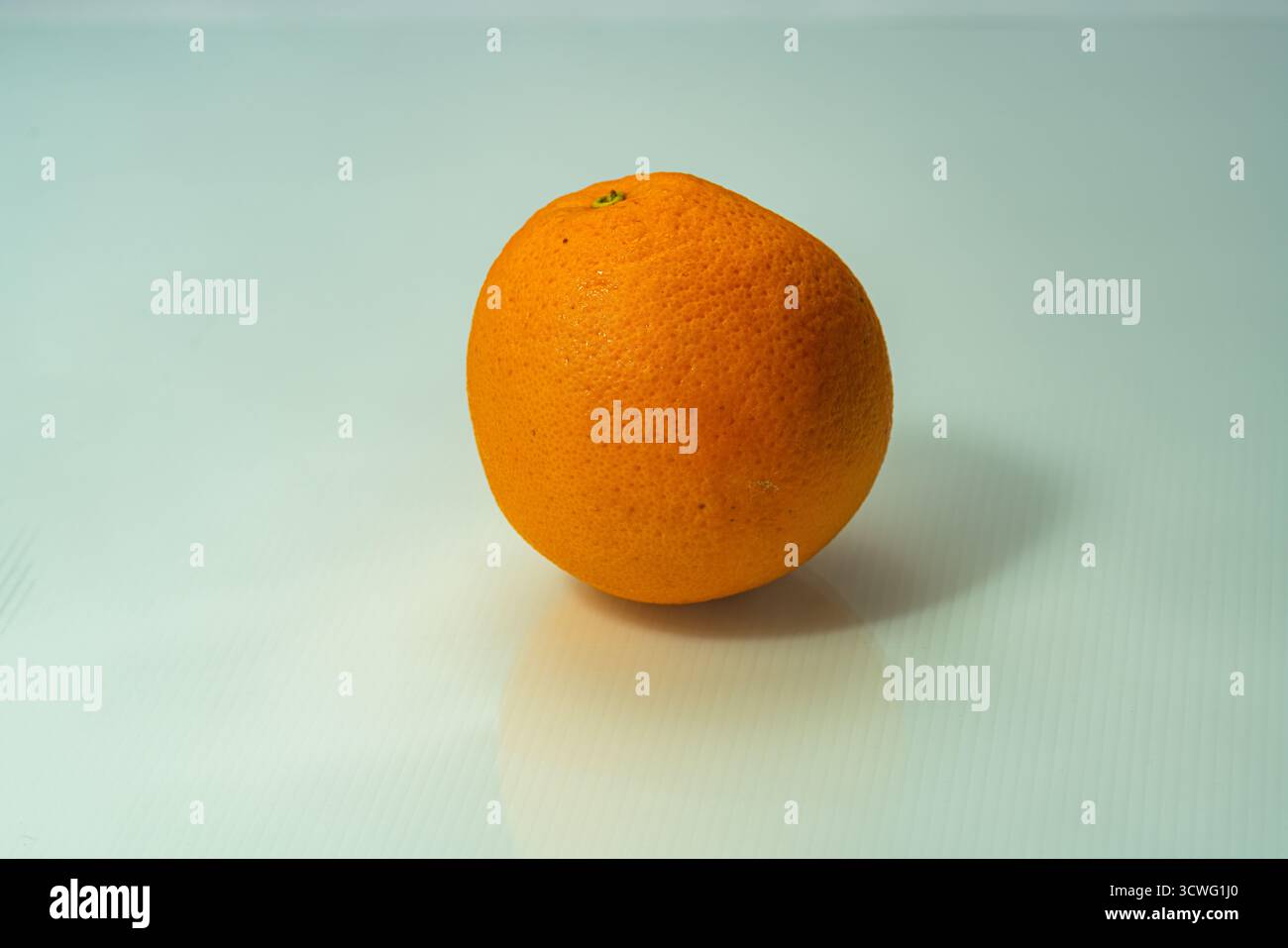 A single orange rests on a pale, clean surface. Its vivid color and ...