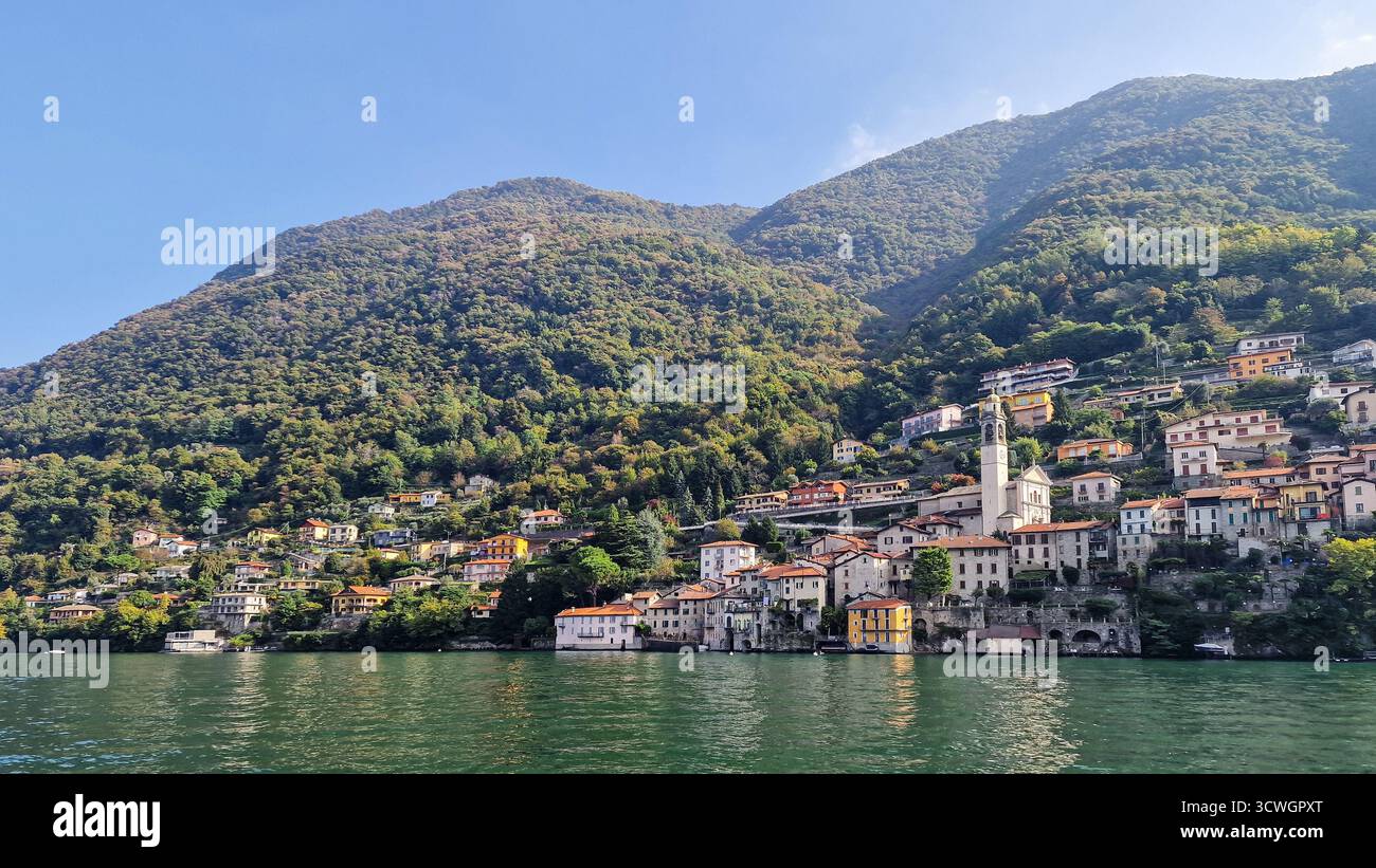 Lakefront village with church bell tower on the forested slopes of Lake ...