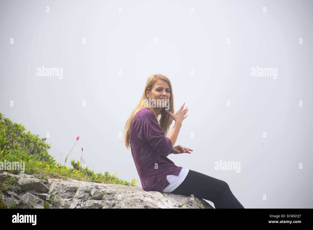 Girl with a stern look on a rock at the top of a mountain in a foggy ...
