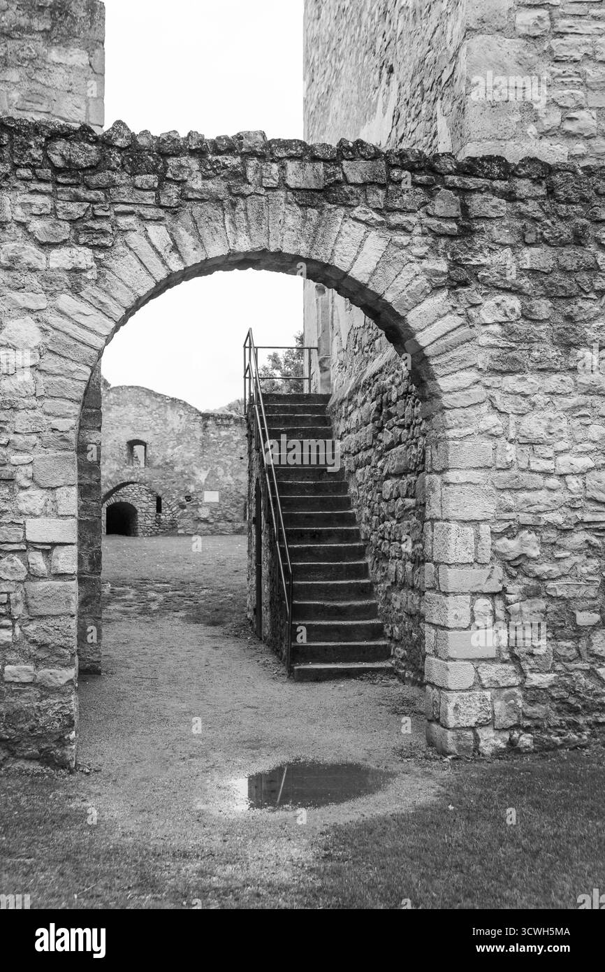 A stone arch with stairs and puddle in a historic building in black and ...