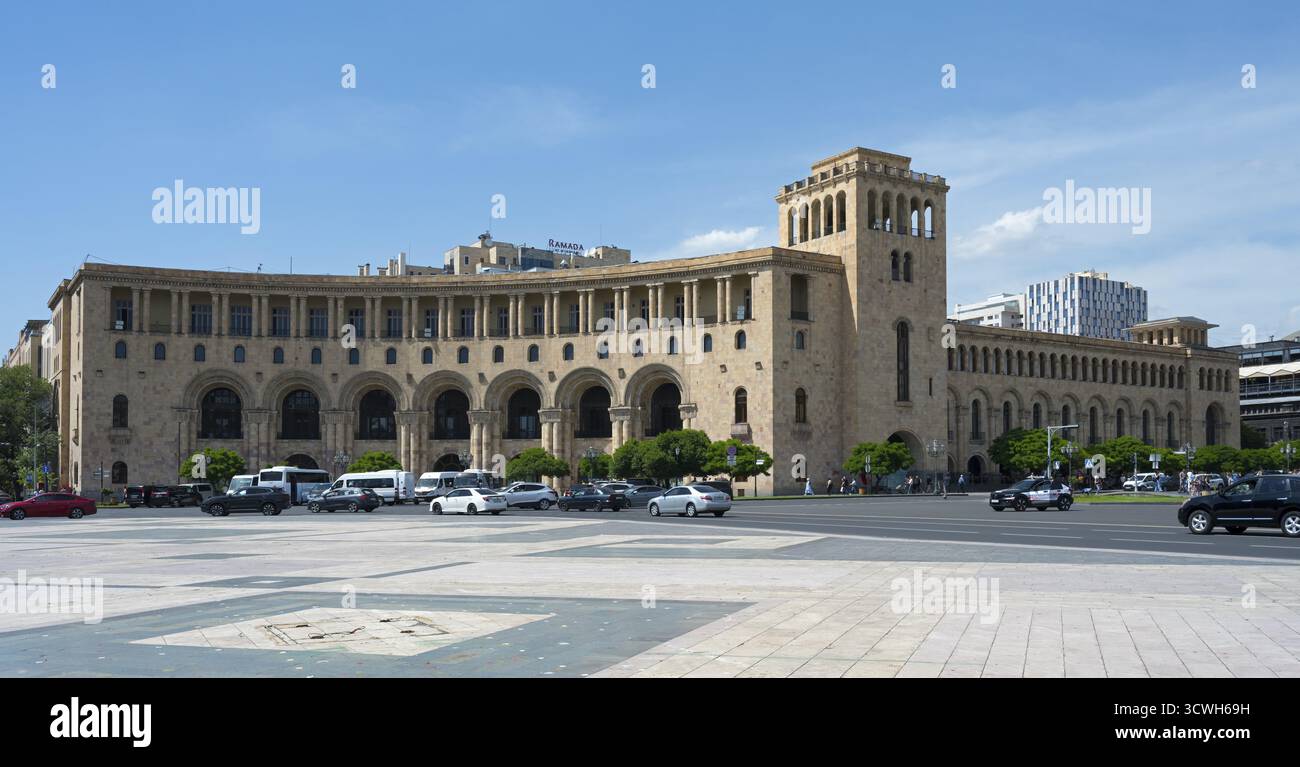 Elongated stone building with arches, in front of which cars are parked ...