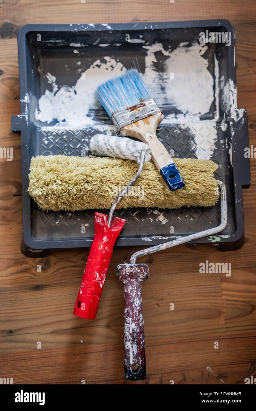 Paint tray with used roller and brush on wooden floor surface during ...