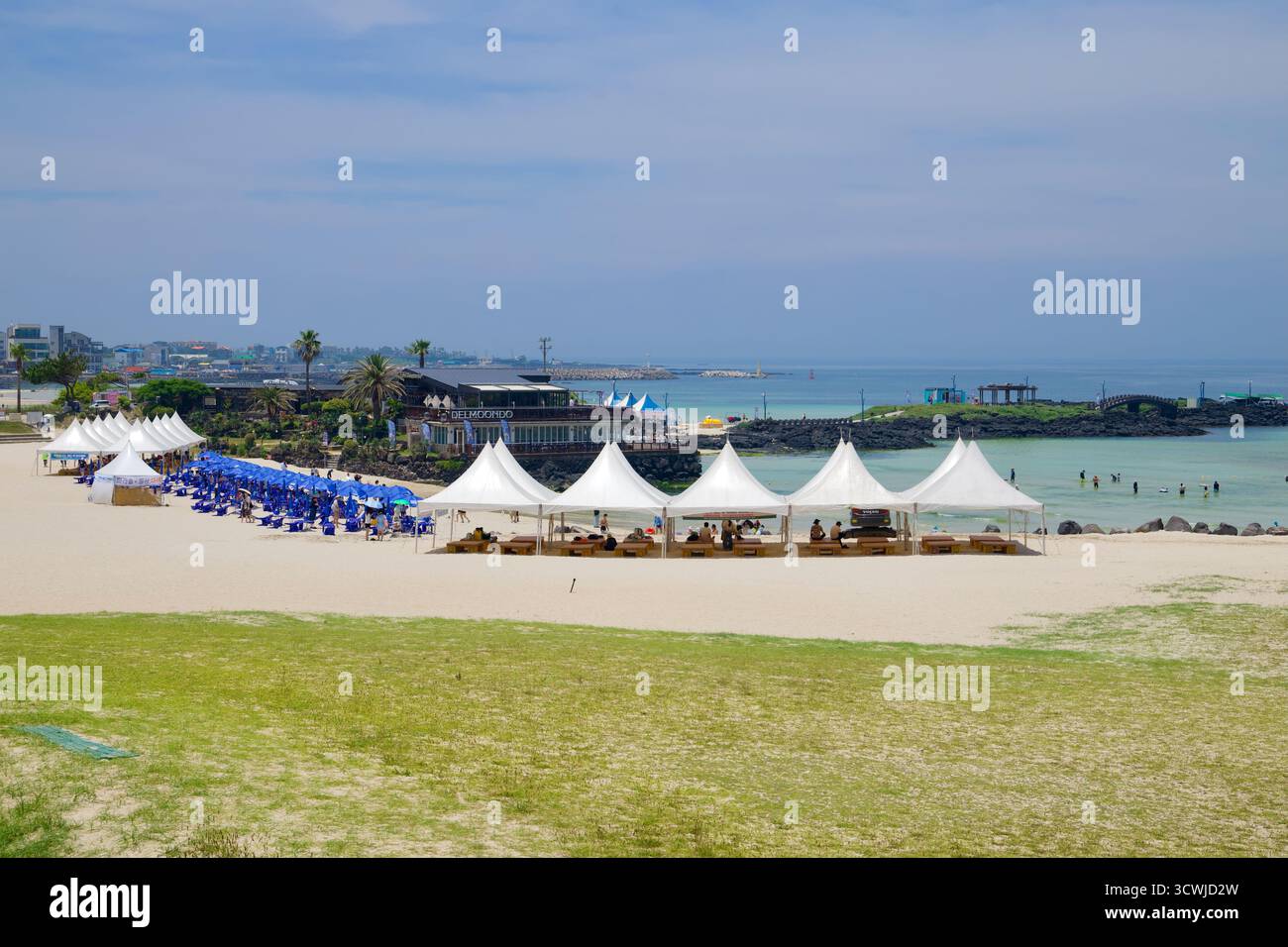Rows of blue parasols and lounge chairs line the wide sand at Hamdeok ...
