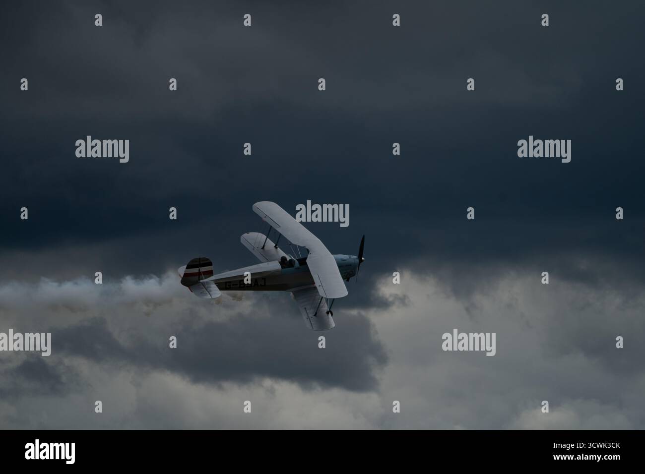 Vintage biplane aircraft flying through dramatic storm clouds at air ...
