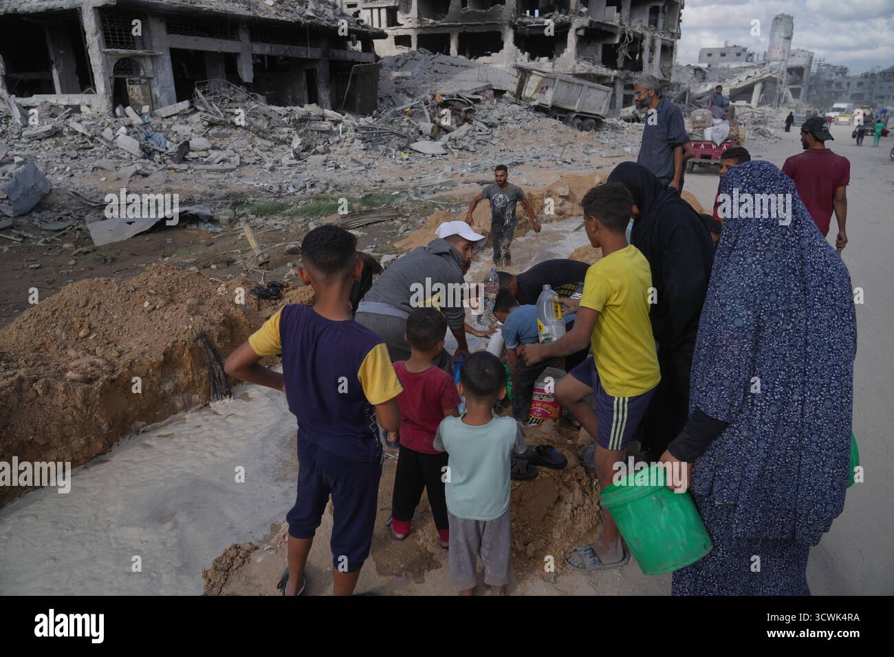 Palestinians collect water from a broken pipe amid destroyed buildings ...