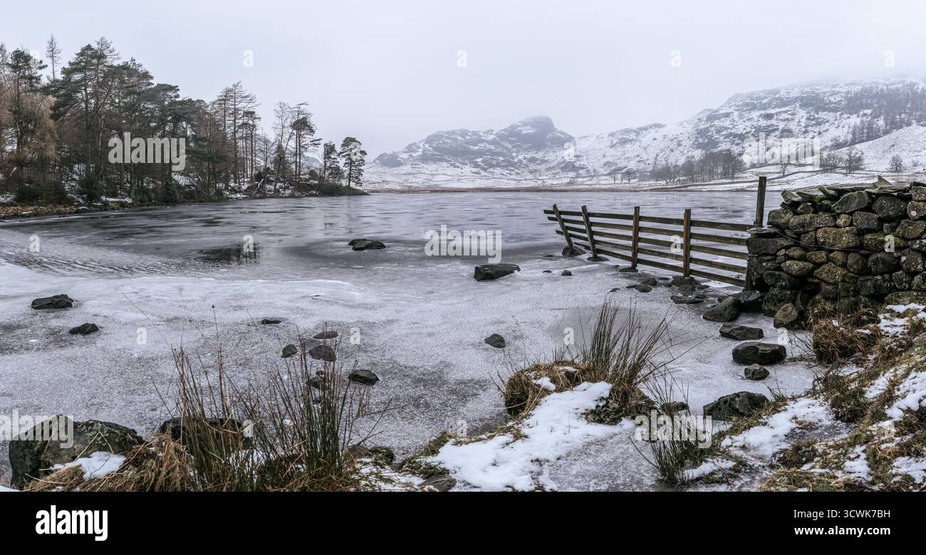 Frozen Blea Tarn with snow-covered fells and wooden fence in winter ...