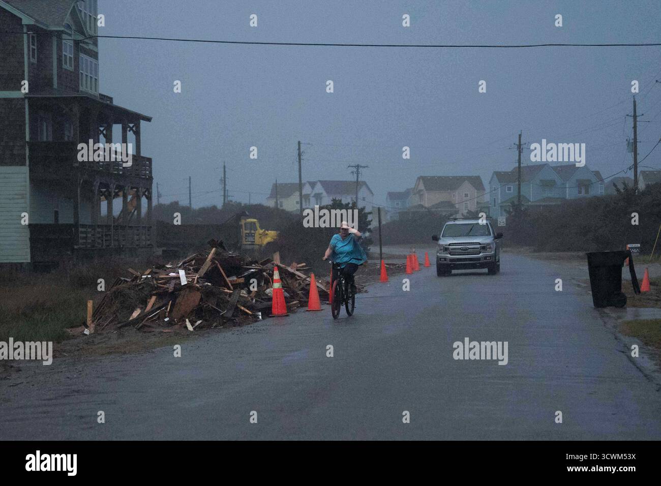 A woman rides a bike past debris in the midst of a storm, Sunday, Oct ...