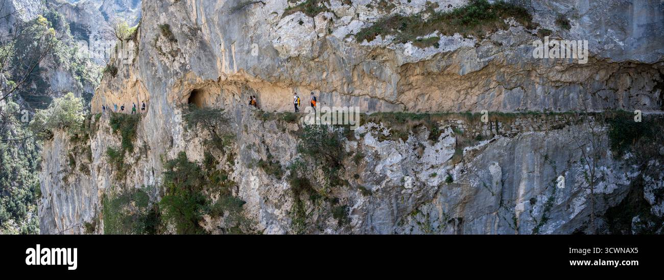 A scenic view of hikers on a narrow trail along a rocky cliffside ...