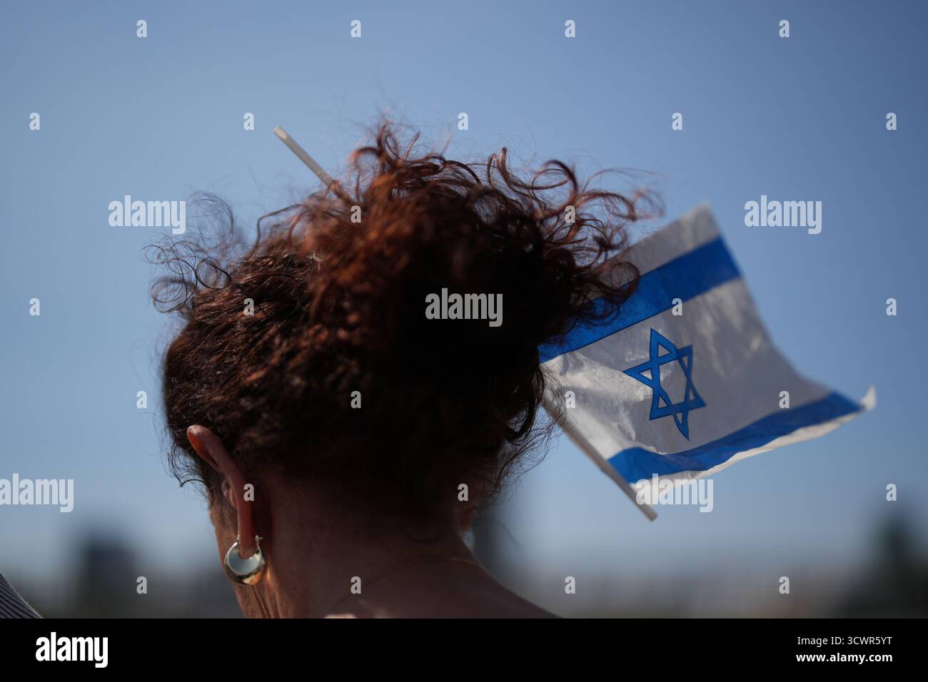 A woman wears an Israeli flag in her hair as she waits outside ...