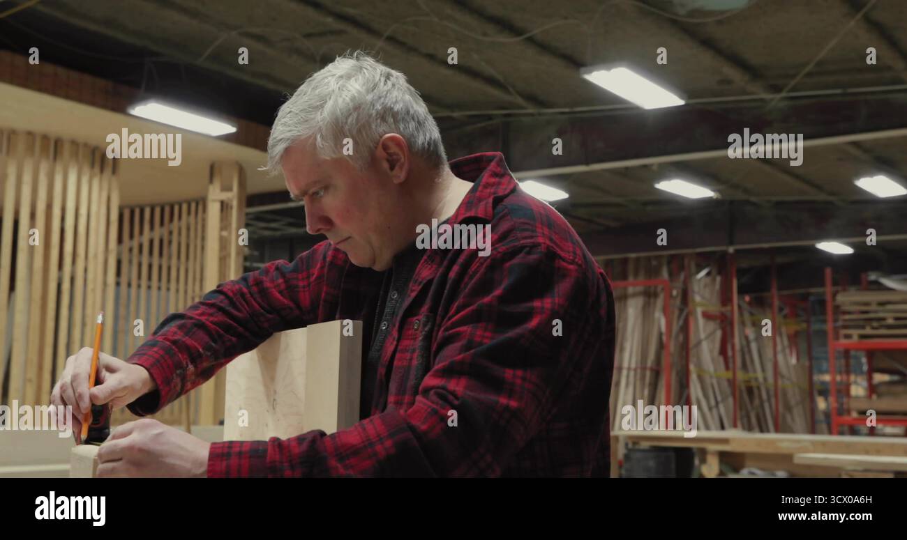 Carpenter wearing flannel marking wooden plank at workbench in wood ...
