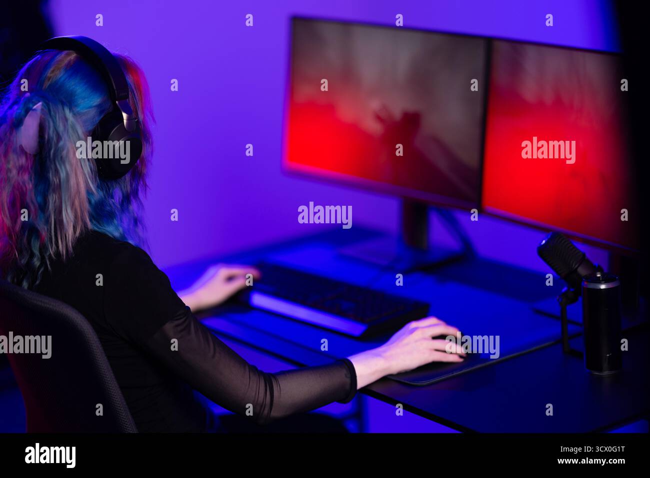 Young woman gaming professionally with dual monitors in illuminated ...