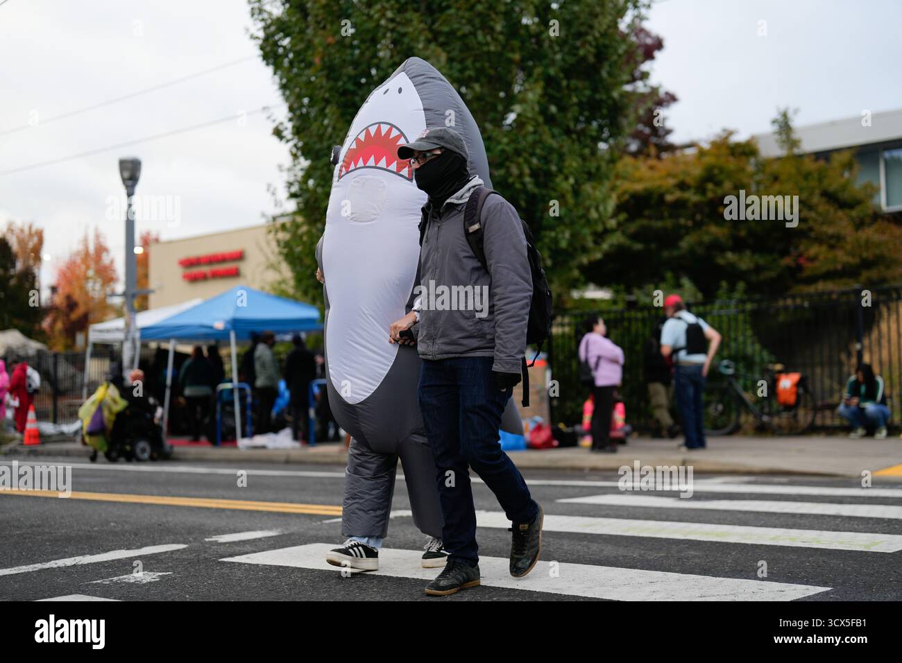 A demonstrator helps a person in an inflatable costume cross the street ...