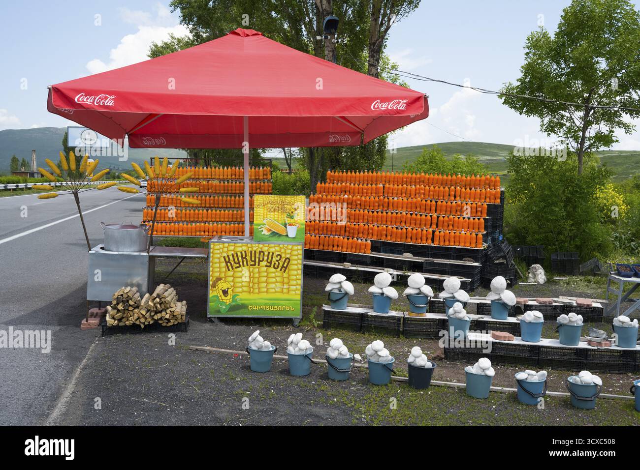 Market stall with juice bottles, buckets and corn under a red parasol ...