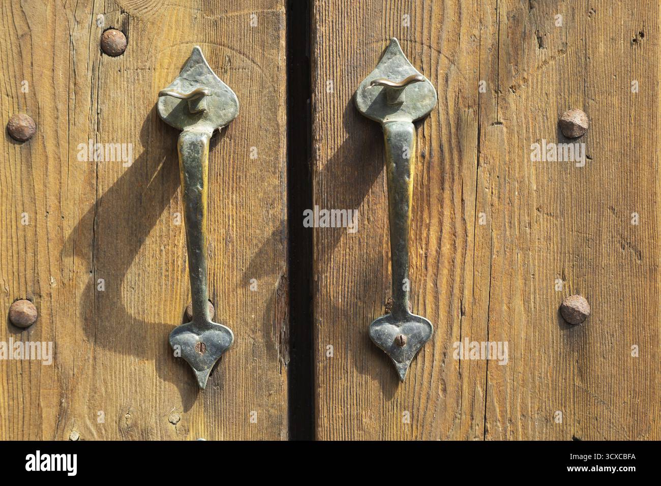 Worn medieval style brass door handles and iron bolt heads on weathered ...