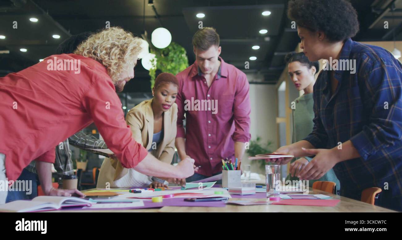 Collaborating six coworkers leaning over conference table with colorful ...