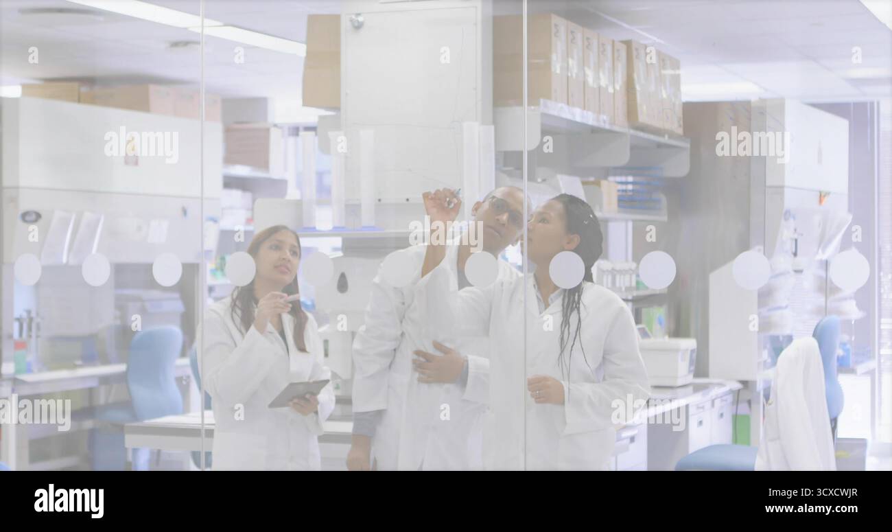 Researchers wearing lab coats collaborating, annotating glass partition ...
