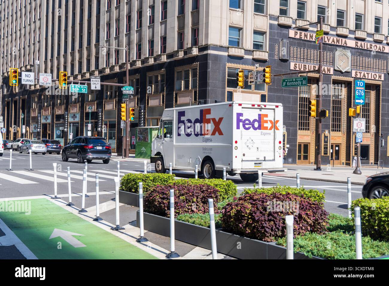 A Fedex truck is driving down a city street. The truck is white and has ...