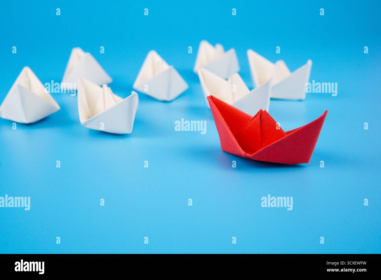 Red paper boat leading white paper boats on blue background ...