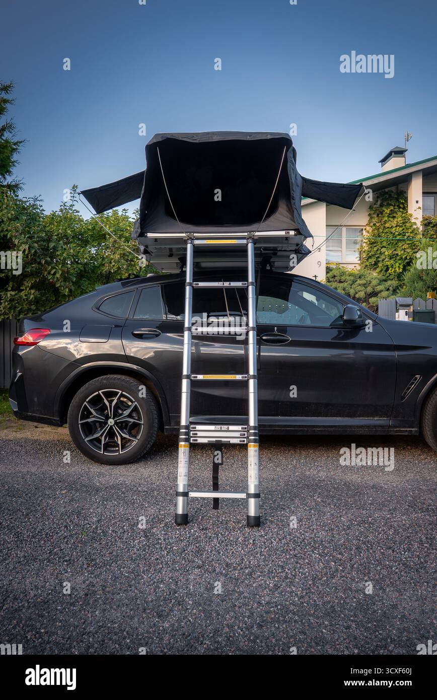 Luxury SUV with rooftop tent and ladder on a quiet neighborhood street ...