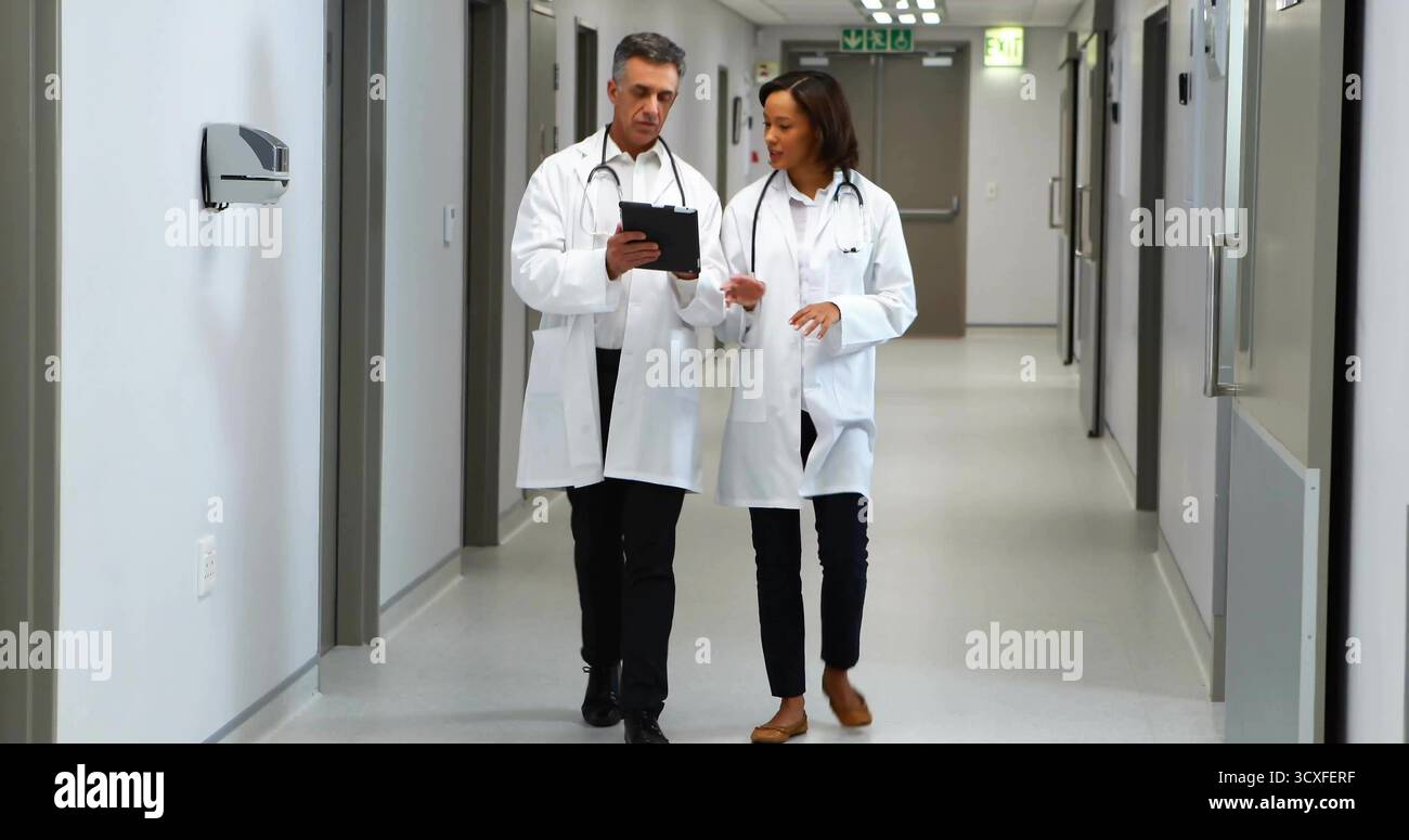 Walking doctor duo reviewing clipboard notes in hospital corridor, with ...
