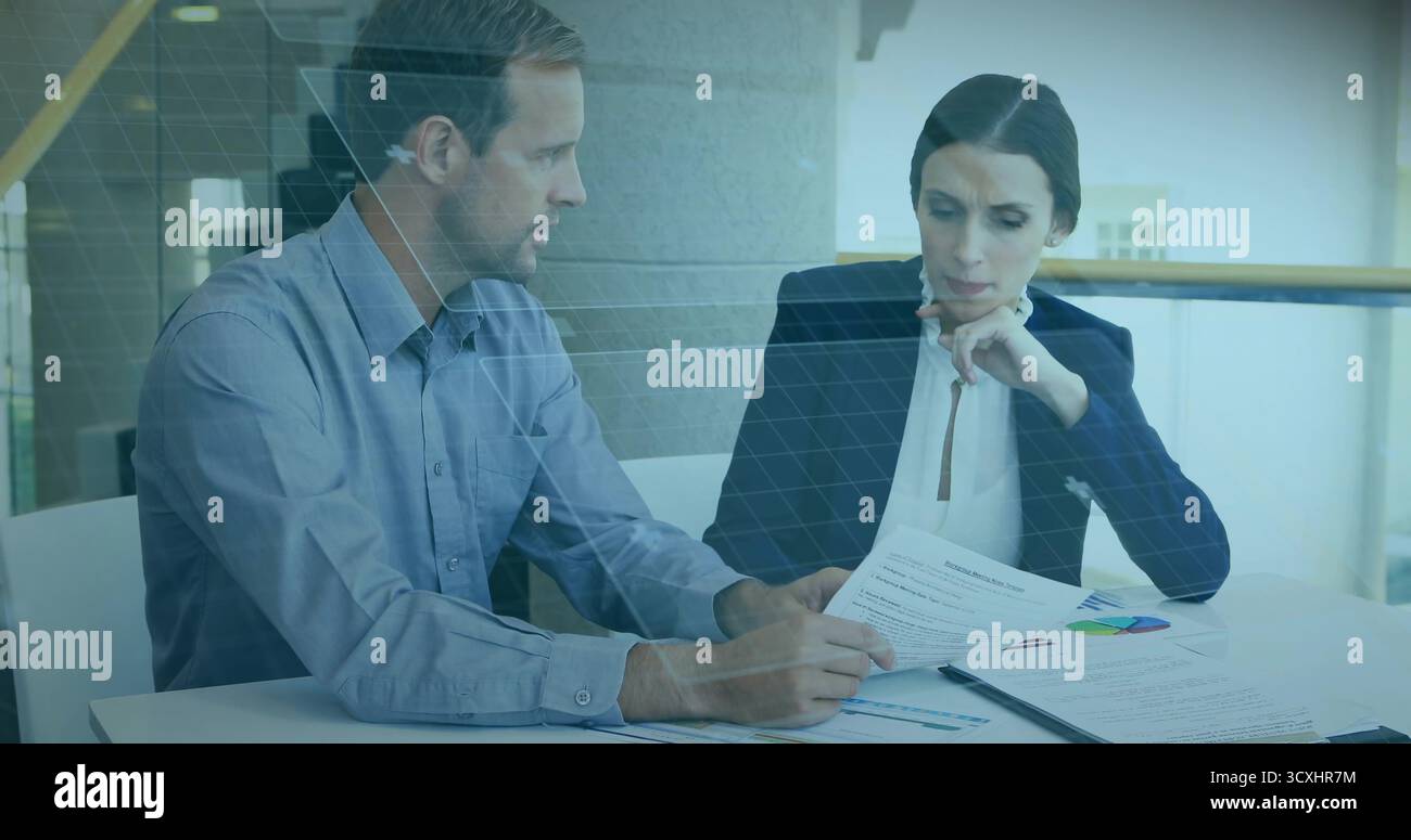 Two colleagues in business attire reviewing printed reports at office ...