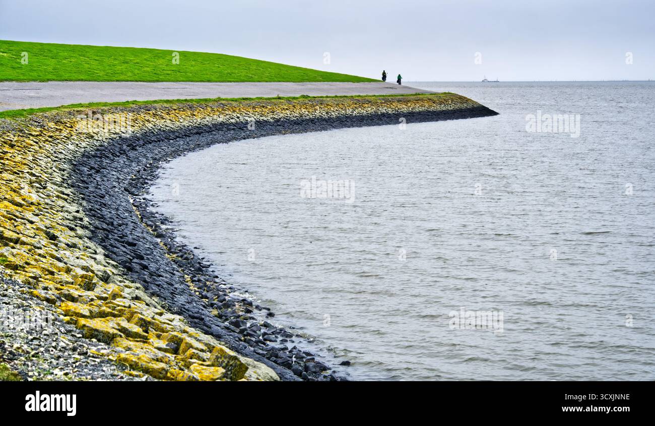 Dike with a paved path curving along the north sea coast, offering a ...